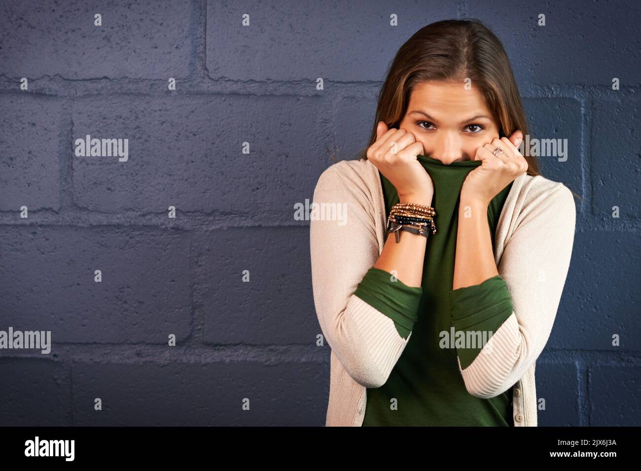 Whoopsie. a young woman covering her mouth against a brick wall ...