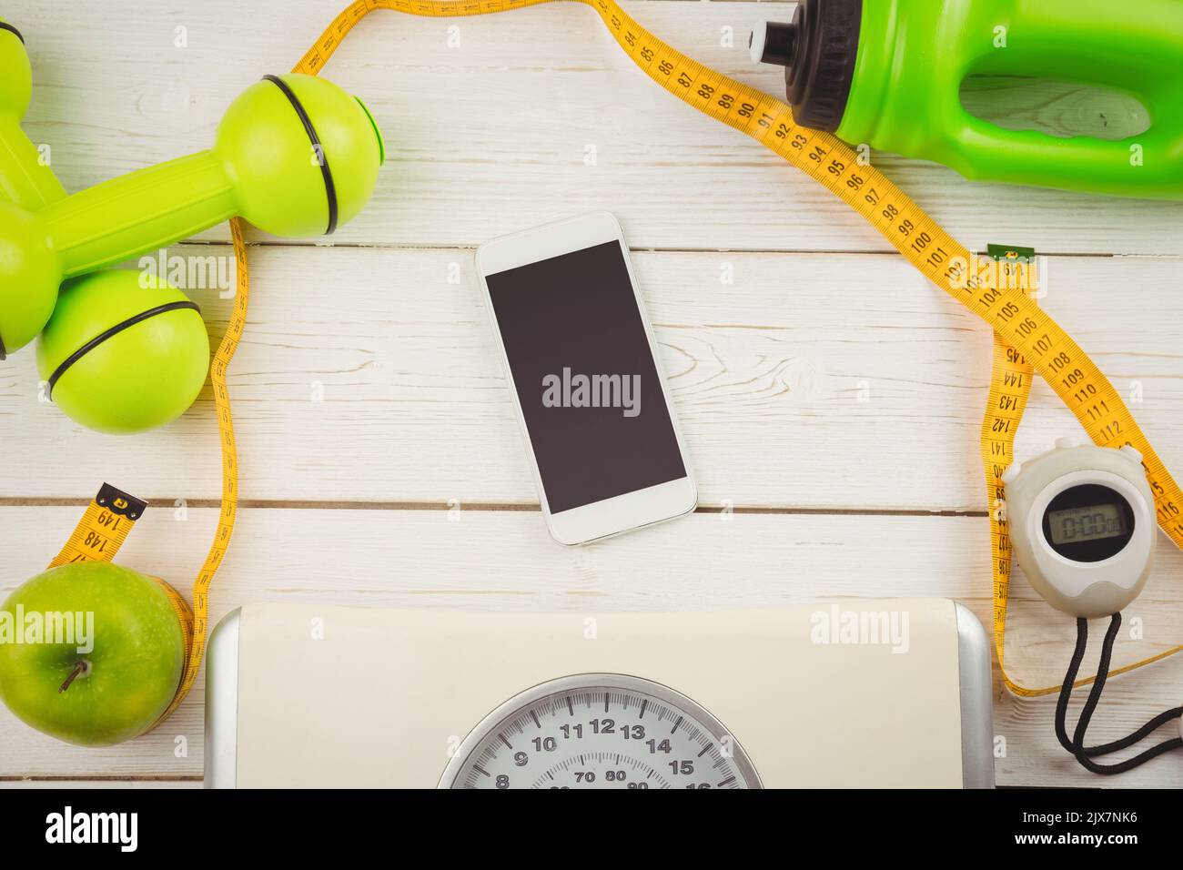 Overhead view of mobile phone and tape measure with dumbbells on table ...