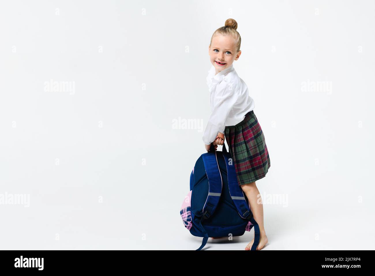 Cute girl in a school uniform with a big and heavy backpack on a white ...