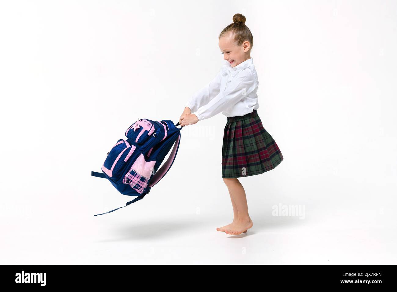 Cute girl in a school uniform with a big and heavy backpack on a white ...