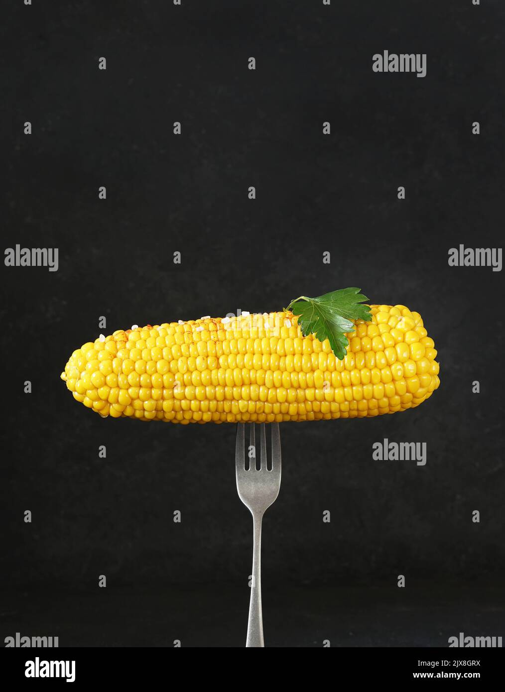 boiled corn on the fork with salt and parsley leaf on dark backround ...