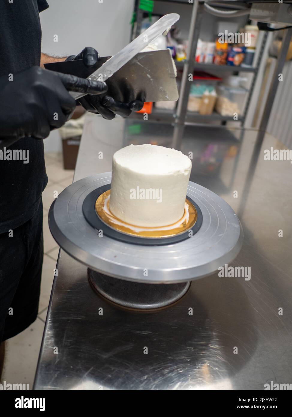 Decorator using spatula and scraper to smooth buttercream on a frosted ...