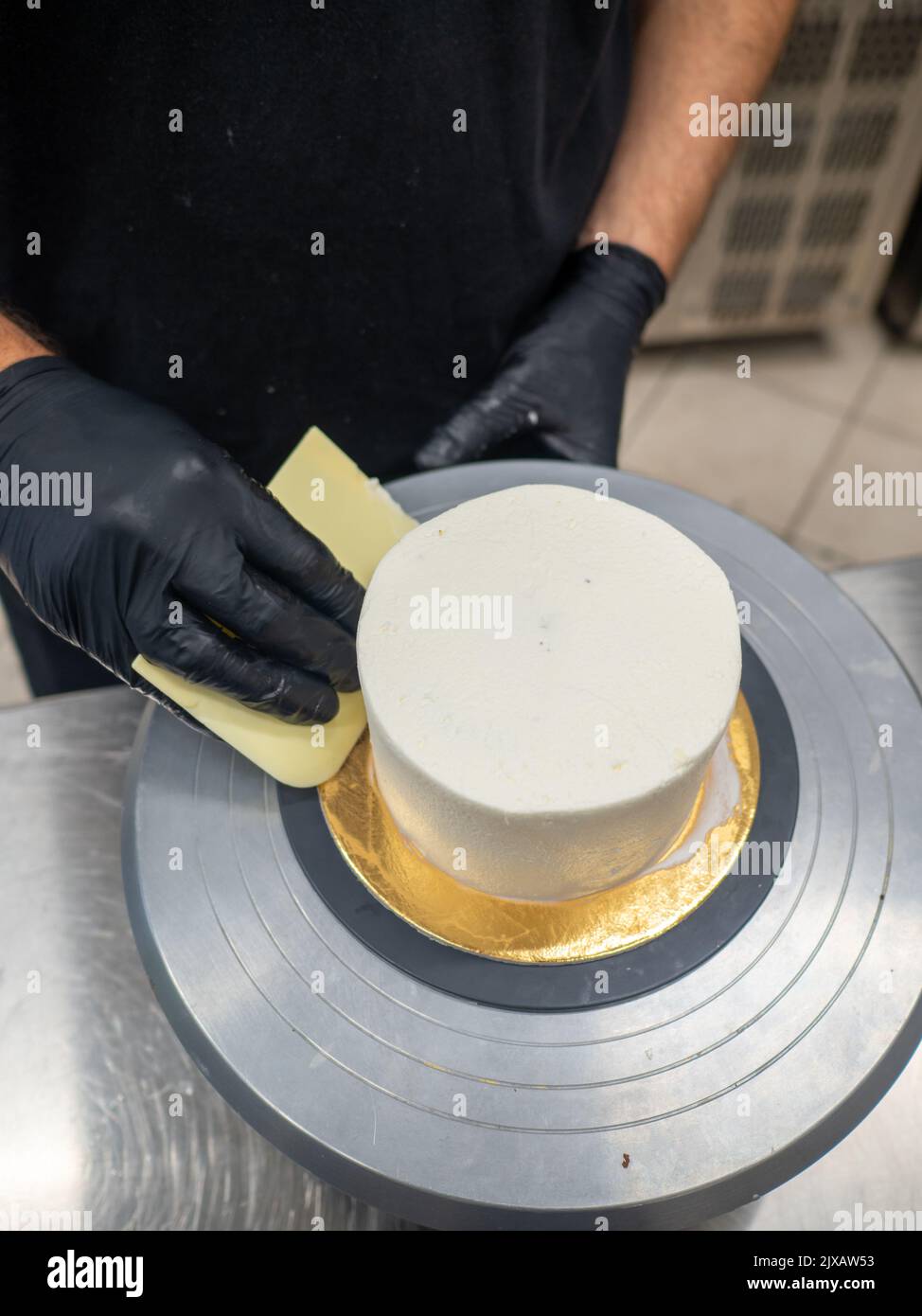 Decorator using spatula and scraper to smooth buttercream on a frosted ...