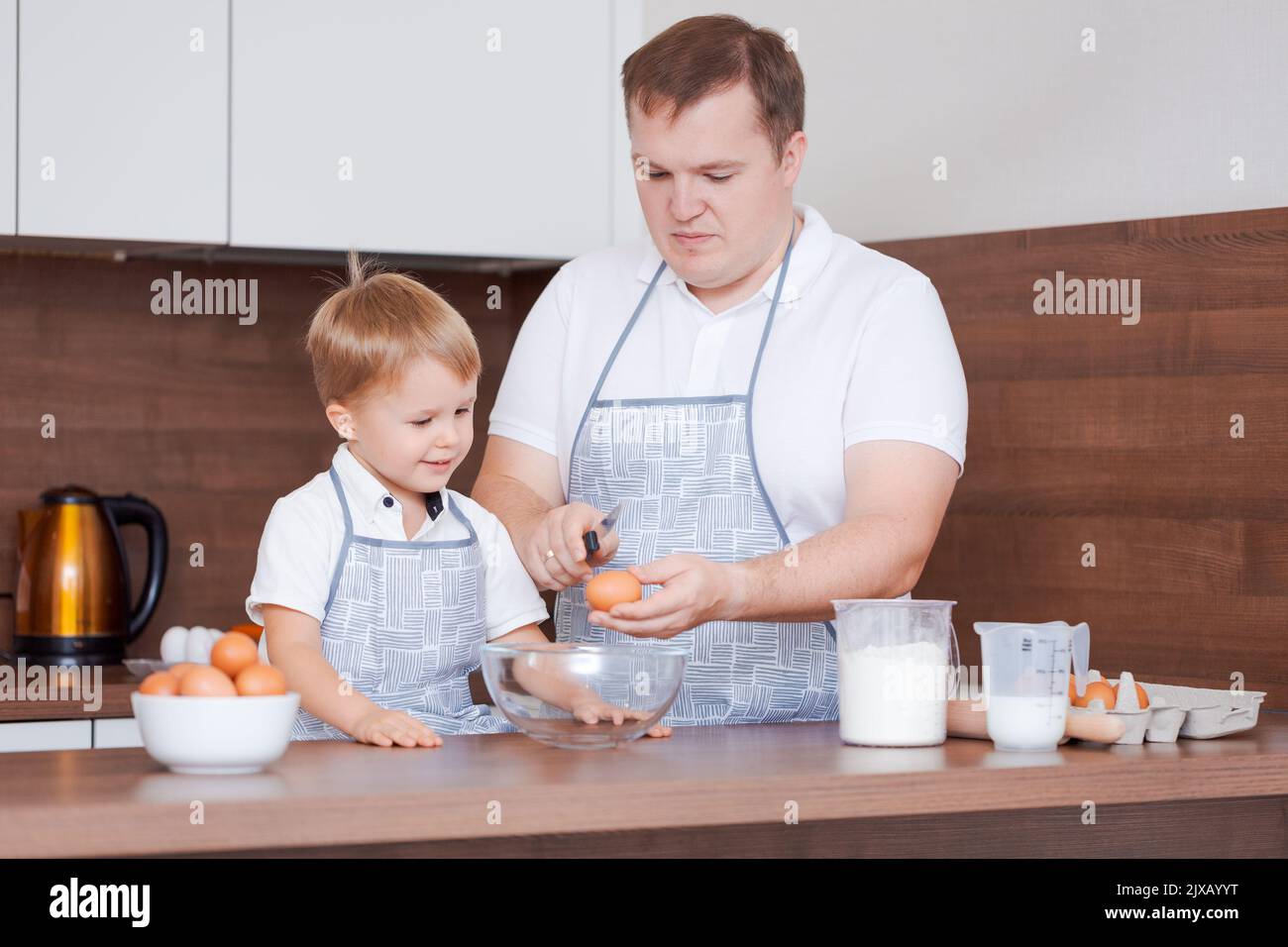 Dad and son in kitchen, father teaches child to break eggs into a bowl ...