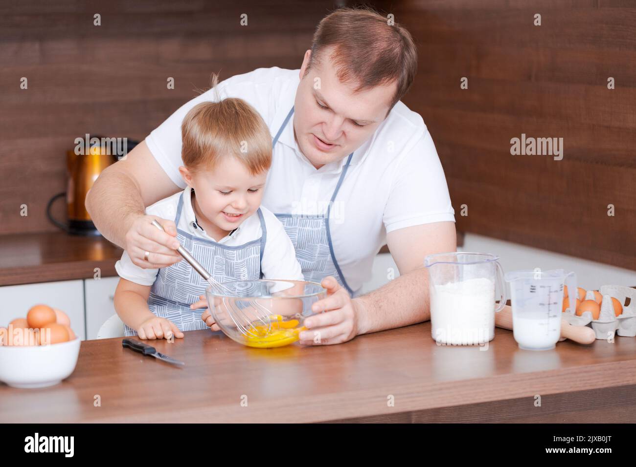 Dad and son in kitchen, father teaches child to break eggs into a bowl ...
