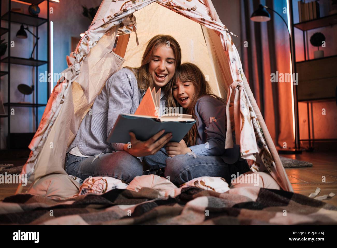 Caucasian pretty blond sisters sitting in wigwam and reading book ...