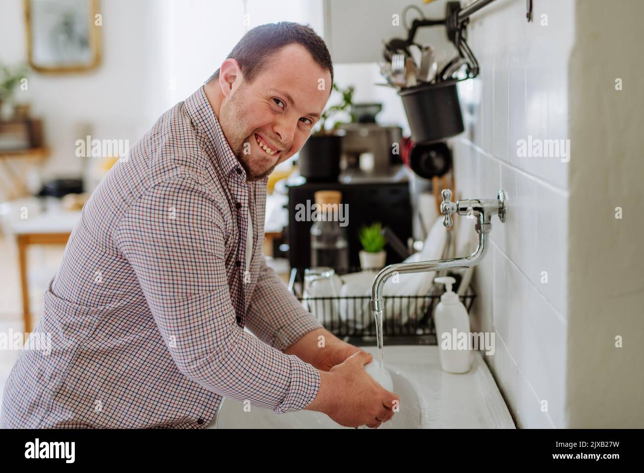 Man with down syndrome washing the dishes, taking care of himself ...