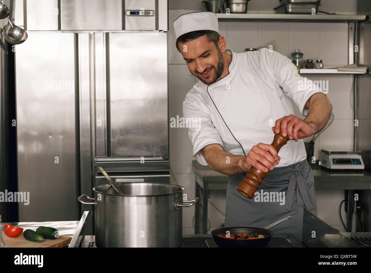 Chef adding salt or pepper to dish while cooking on restaurant kitchen ...