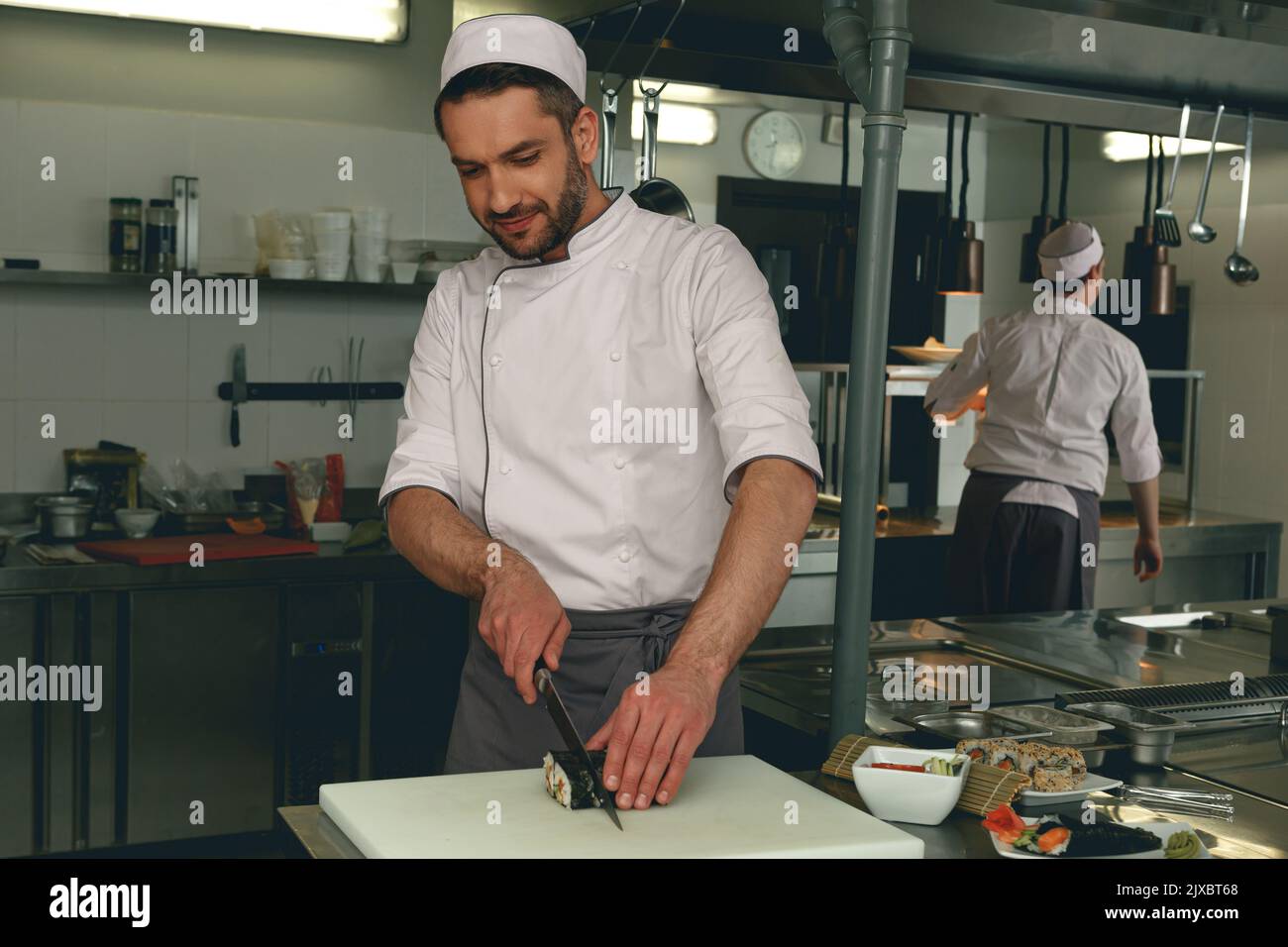Smiling Male Chef in uniforms preparing sushi in a kitchen of asian ...