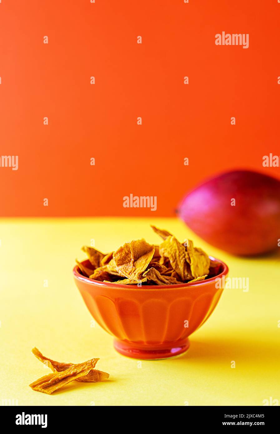 Mango chips in bowl over yellow and orange background Stock Photo - Alamy