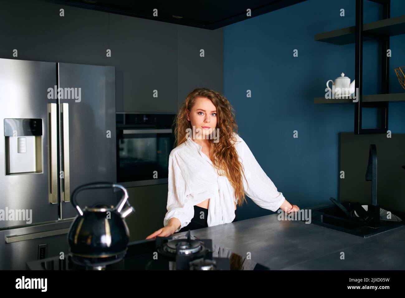 Portrait of blonde caucasian woman standing and smiling in her kitchen ...