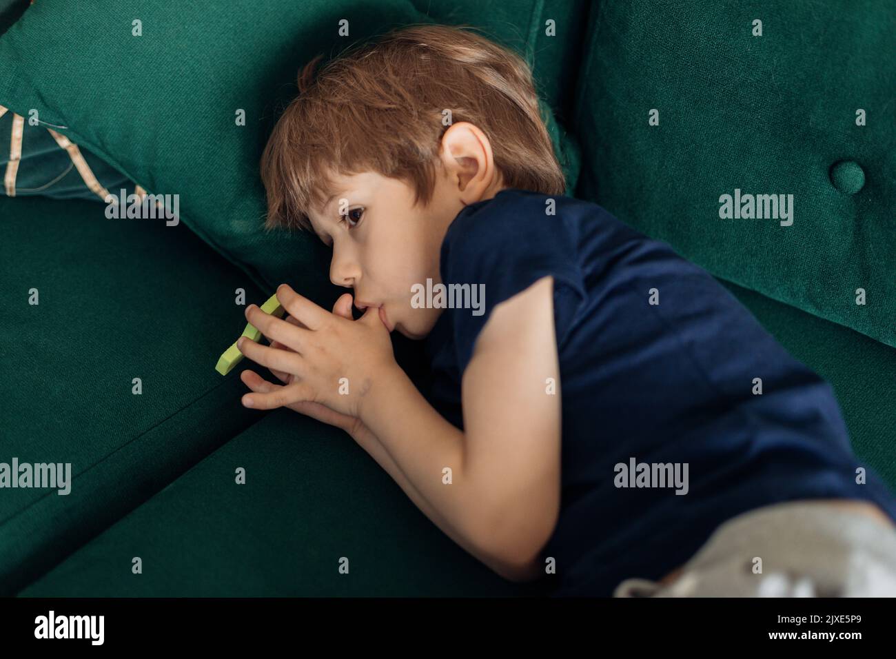Portrait of serious, scary, sad and depressed little boy lying on green ...
