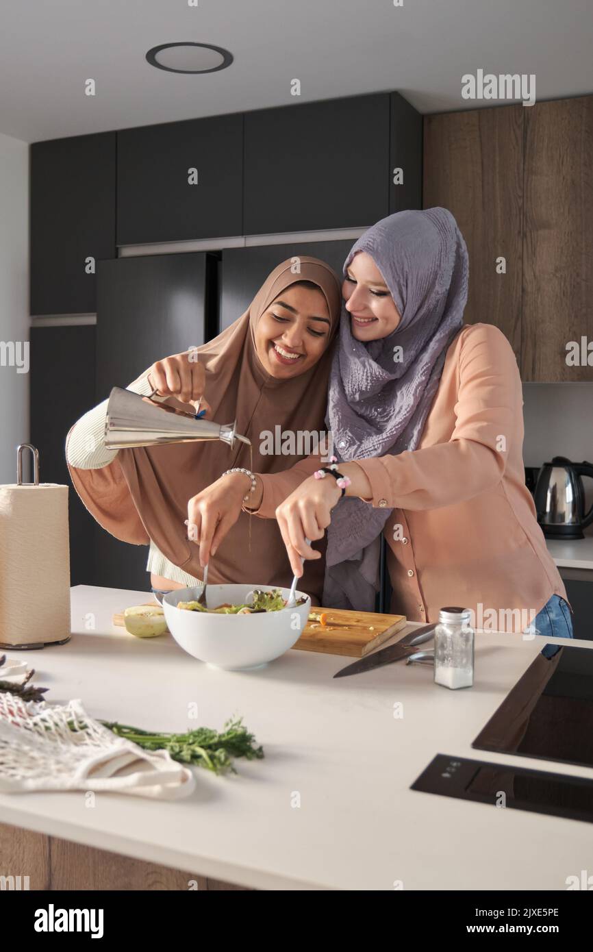 Two muslim friends smile while pouring olive oil and tossing a salad at ...