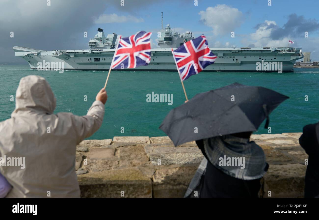 People wave from the shore as the Royal Navy aircraft carrier and ...