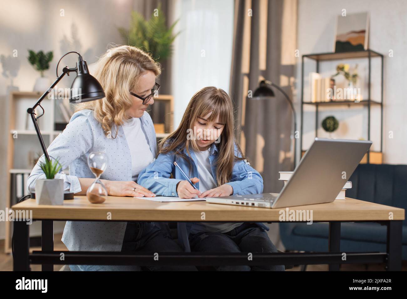 Young caucasian mother helping daughter remote studying at home ...