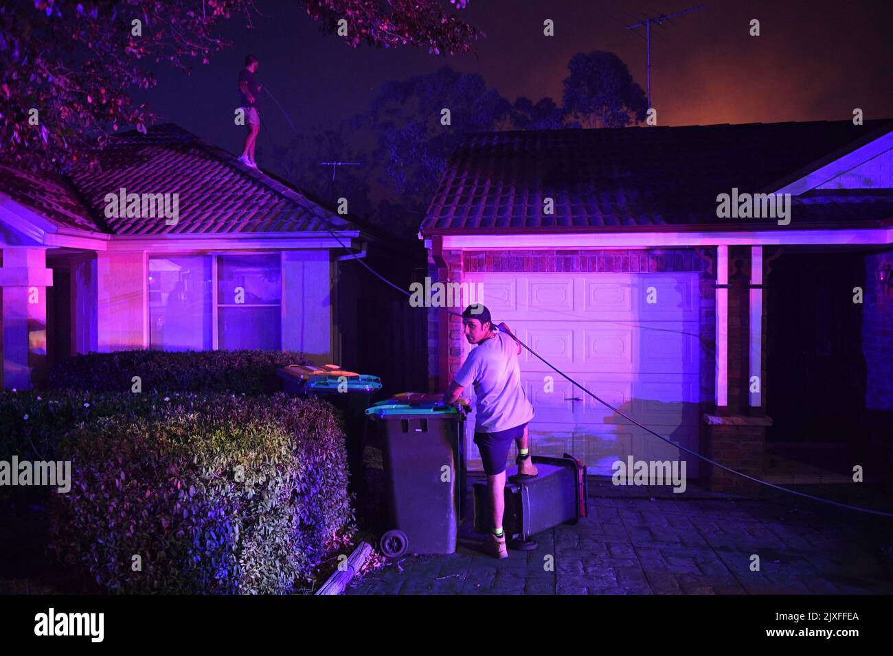 Local resident Jordan Dodin climbs onto a roof to protect the house ...