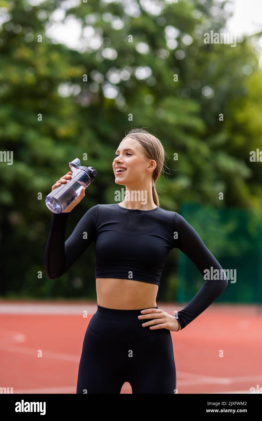 Shot of beautiful female runner standing outdoors holding water bottle ...