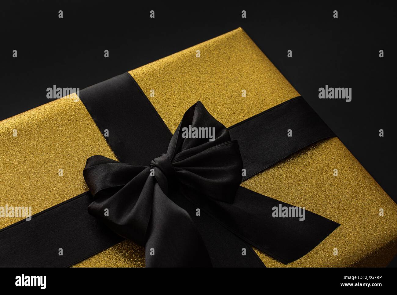 Gift box in a golden wrapper with a black bow close-up on a black ...