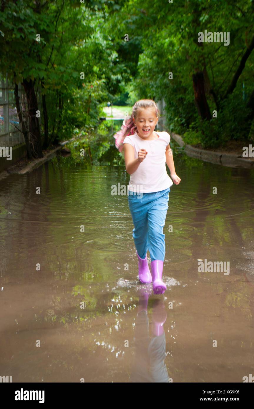 A happy braided girl in rubber boots is jumping and running in muddy puddles Stock Photo - Alamy