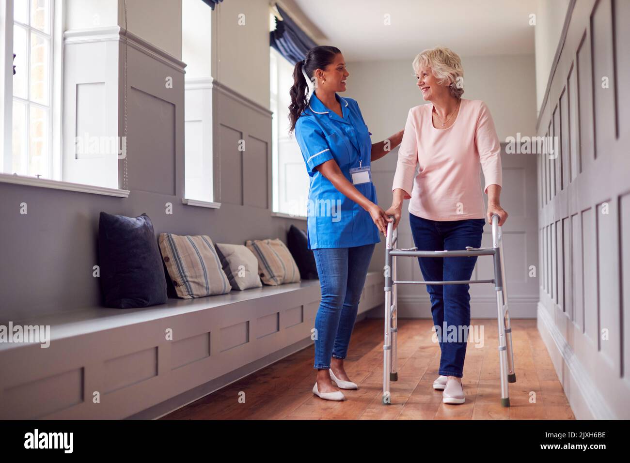 Senior Woman At Home Using Walking Frame Being Helped By Female Care ...