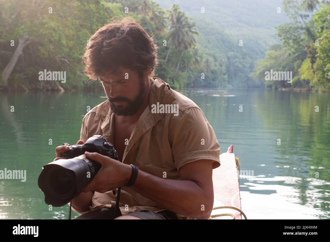 Adventurer photographer in tropical jungle on canoe reviewing images on ...