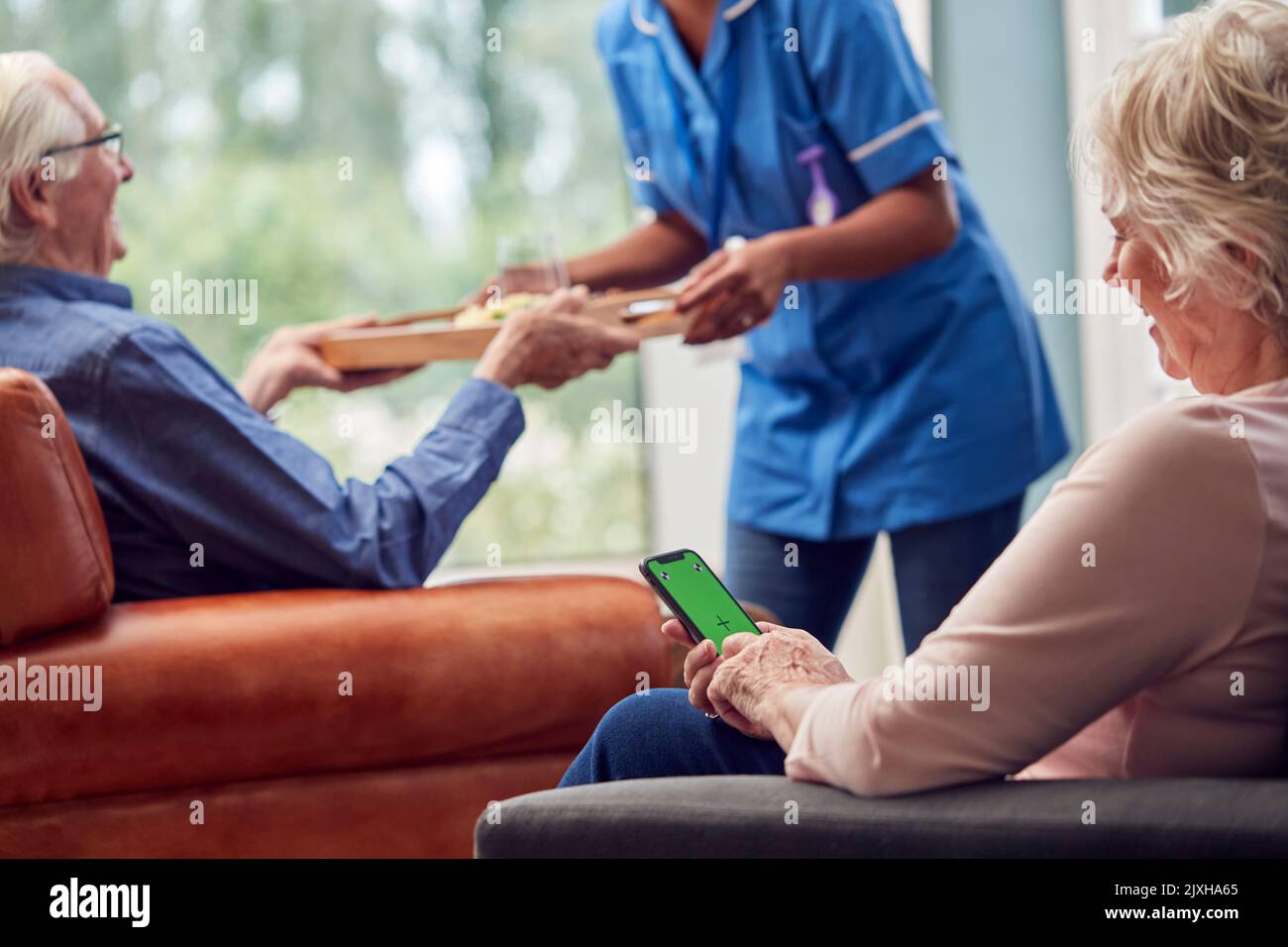 Close Up Of Senior Woman Using Mobile Phone As Carer Brings Meal To ...