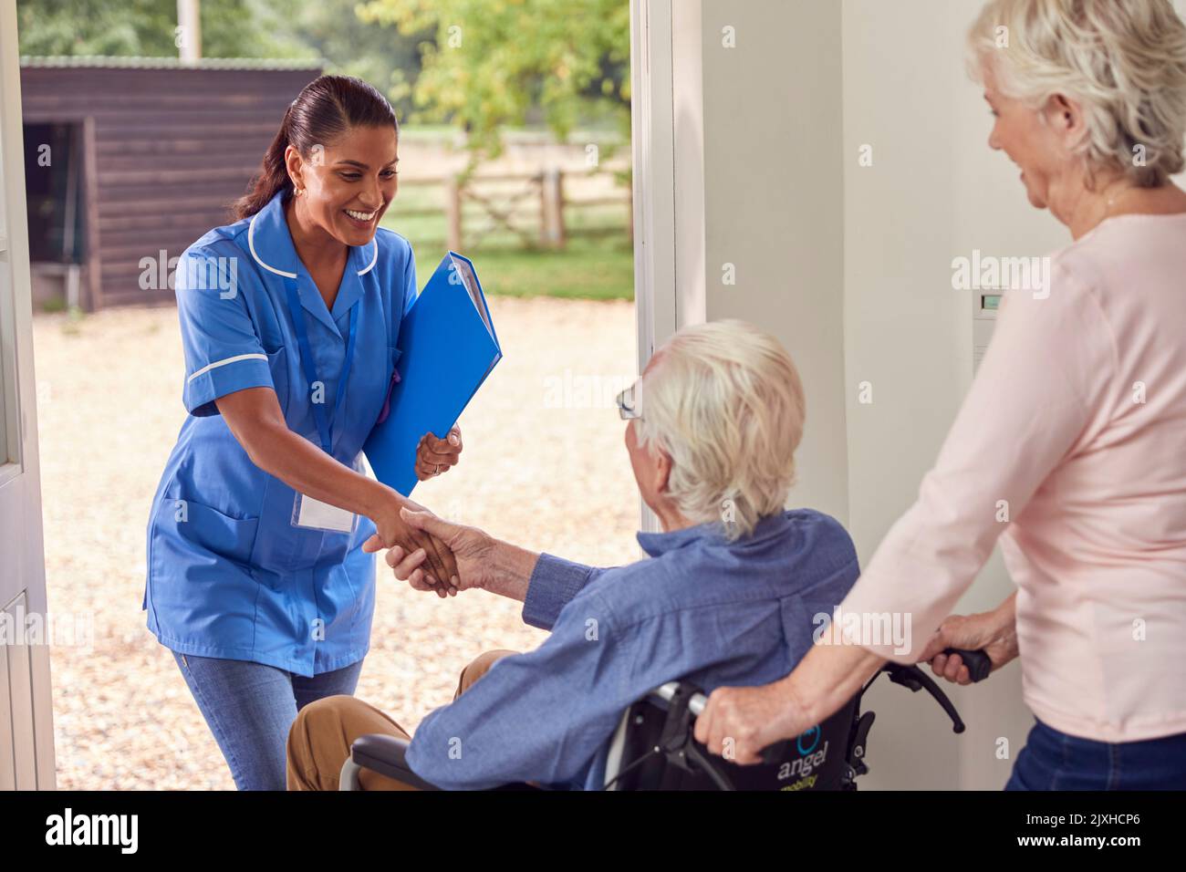 Senior Couple With Man In Wheelchair Greeting Female Nurse Or Care ...