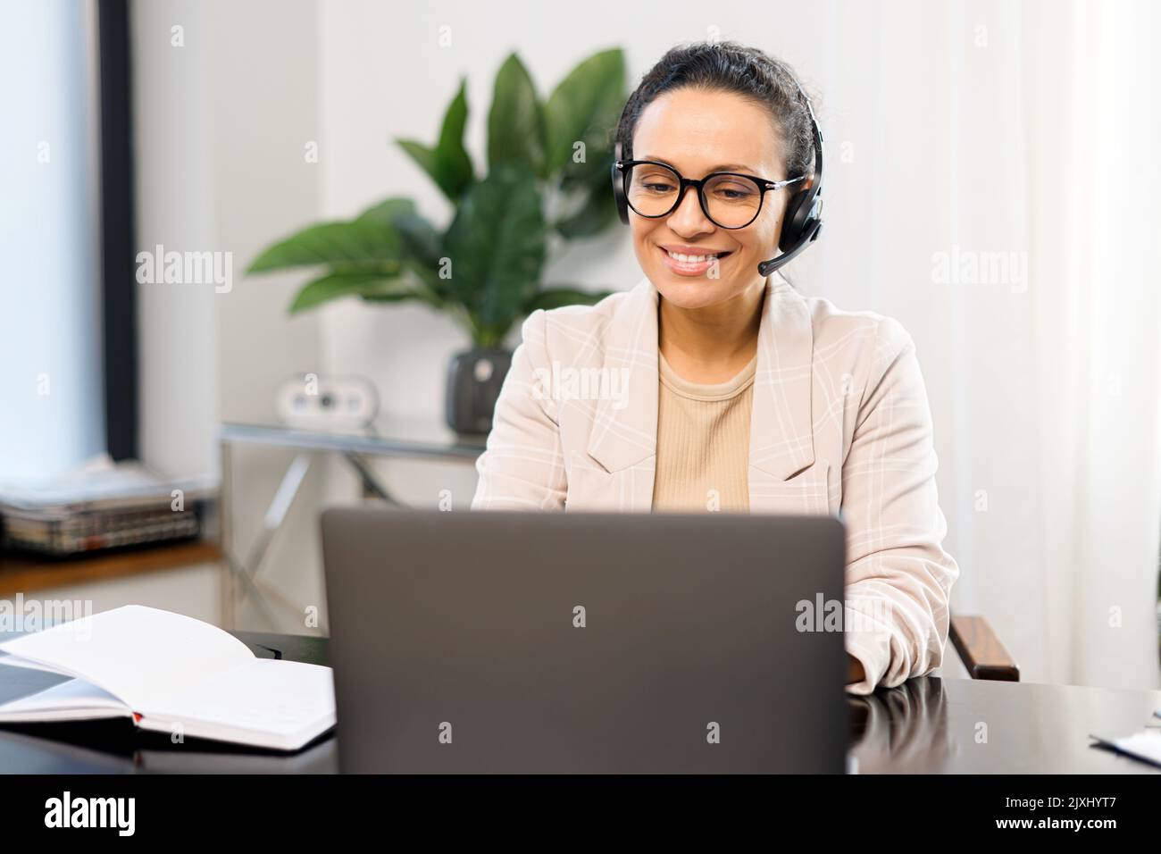 Smiling female call center employee using a headset and laptop for ...