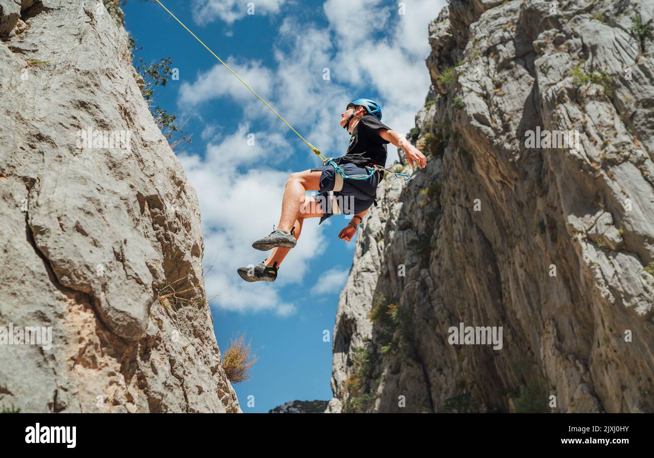 Climber teenager boy in protective helmet abseiling from vertical cliff ...