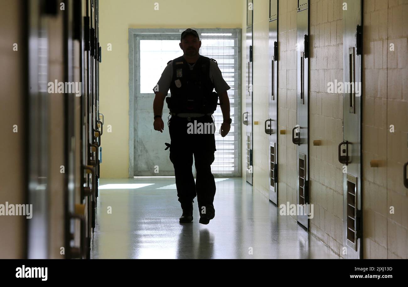 A corrections officer walks down a cell corridor. Prison stock at ...