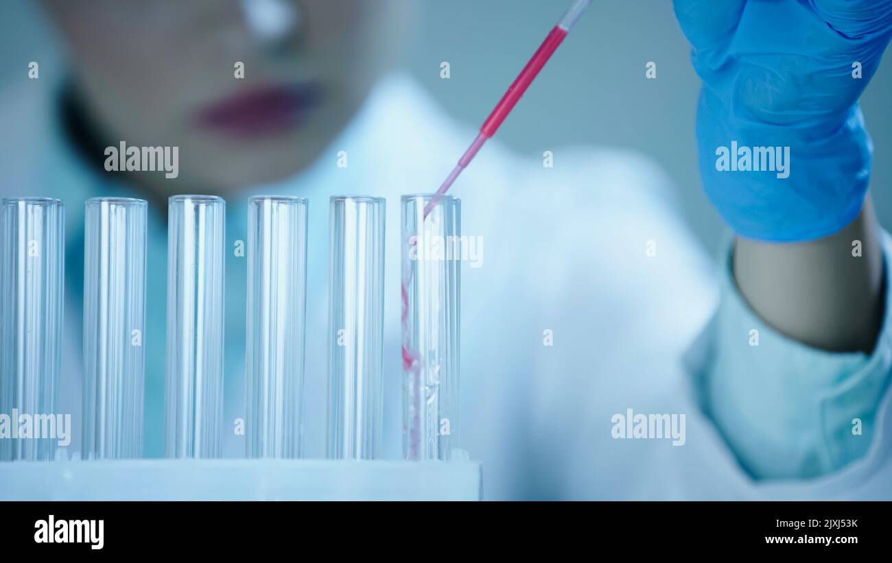 partial view of blurred scientist adding red sample into clean test ...