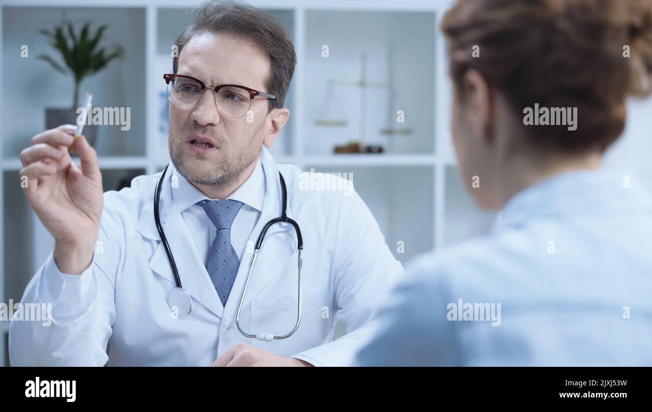 serious doctor in glasses holding cigarette while warning blurred ...