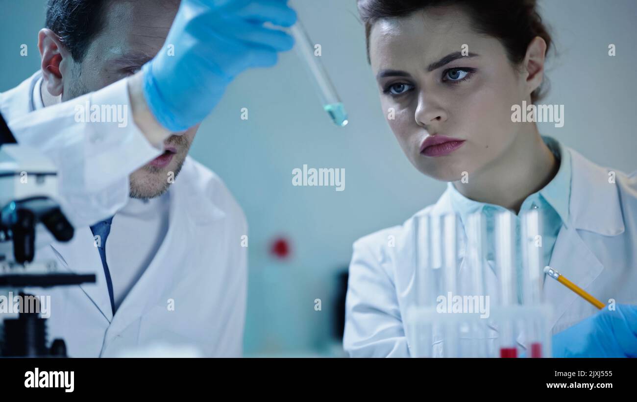 two scientists in white coats looking at test tube with sample in ...