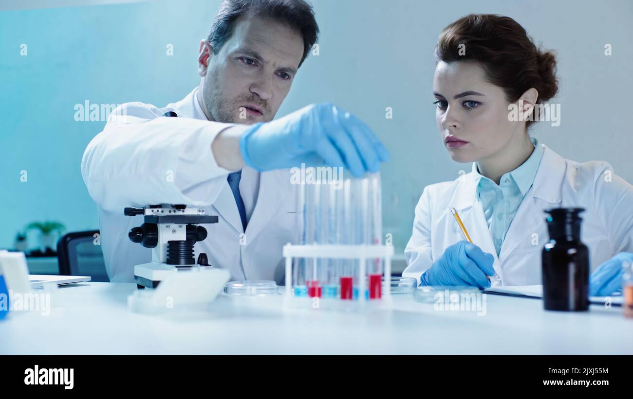 scientist taking test tube with sample near colleague with pencil in ...