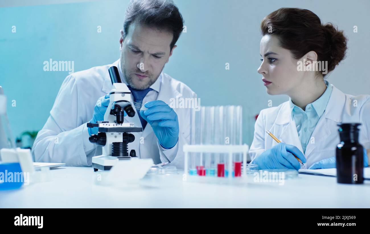 scientist holding glass with sample near colleague in white coat ...
