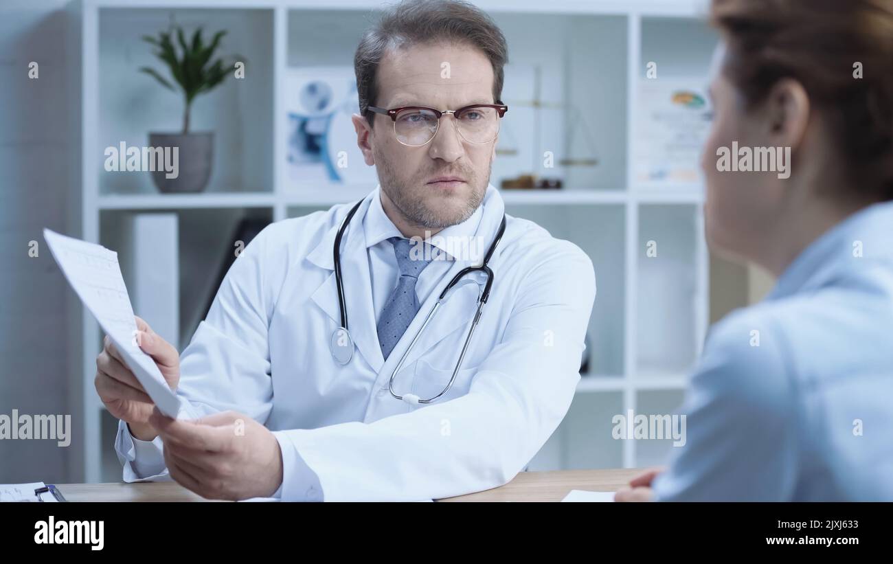 cardiologist in glasses and white coat holding cardiogram and talking ...