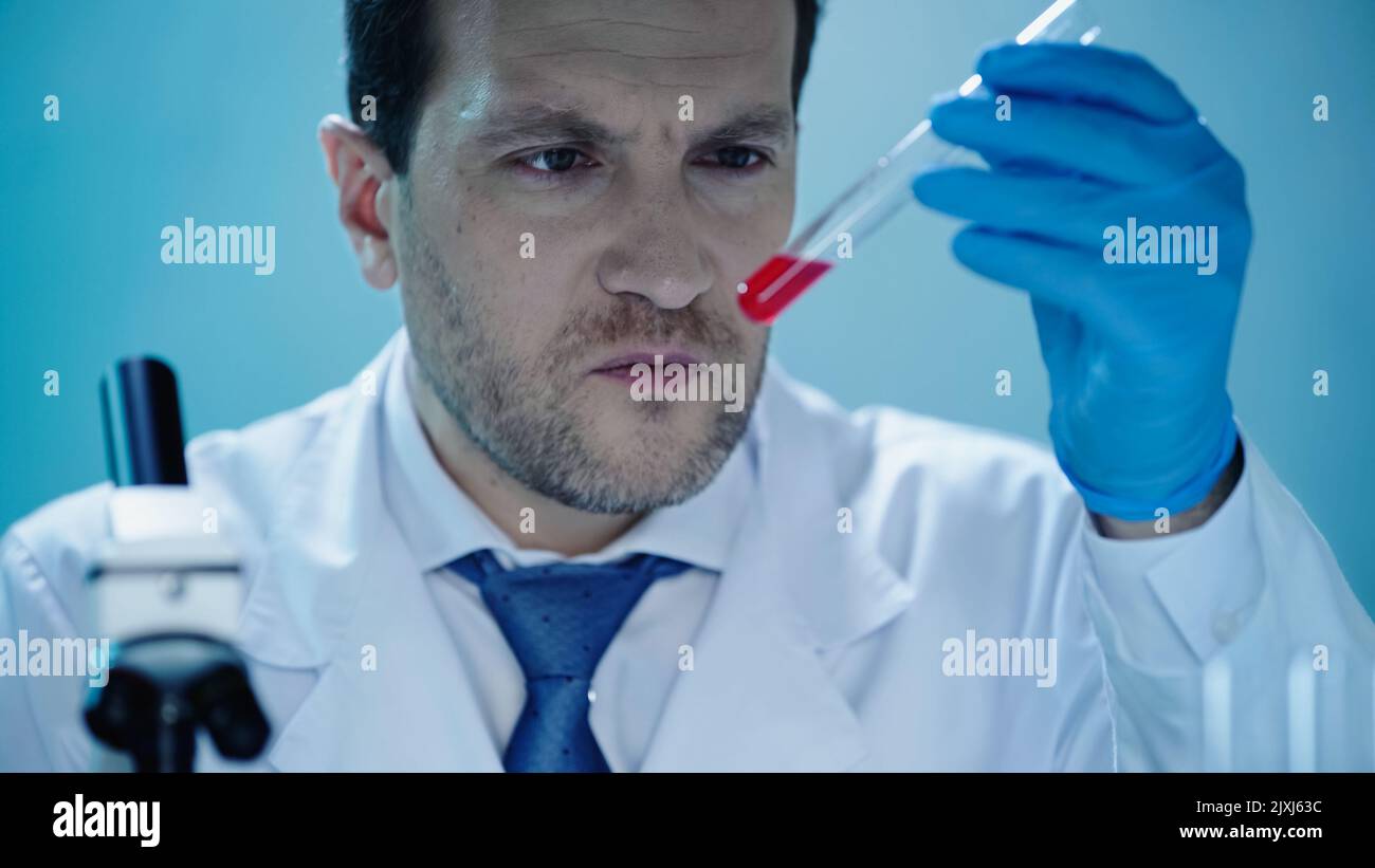 male scientist looking at test tube with red liquid in clinical ...