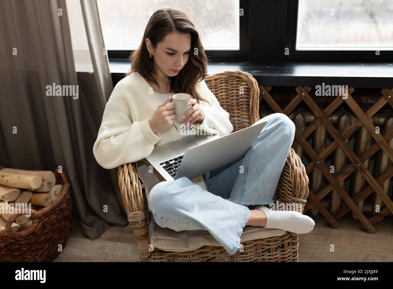 a young woman sits on the couch with her legs tucked under her with a ...
