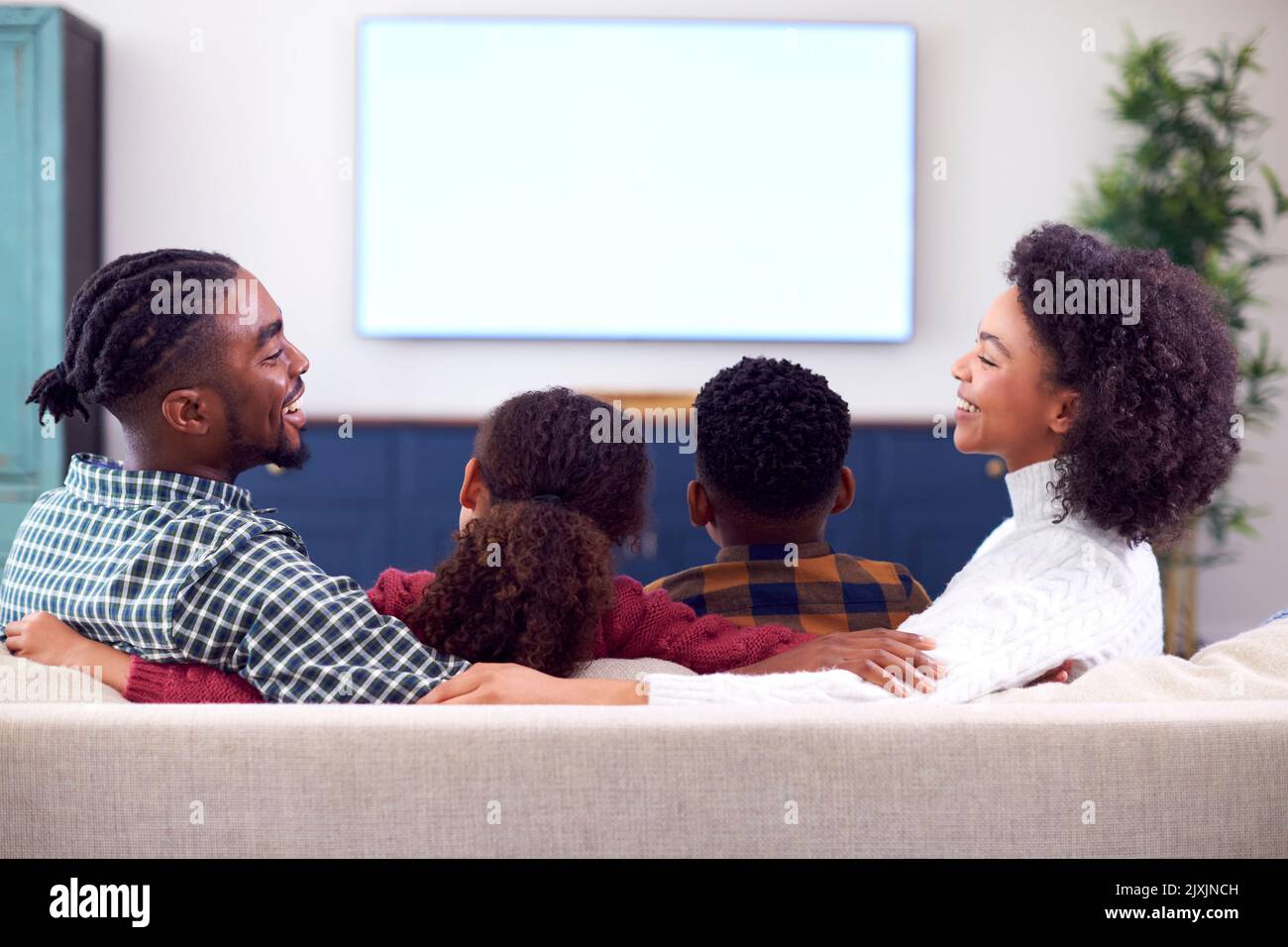 Rear View Of Family Sitting On Sofa Watching Movie On TV At Home Stock ...
