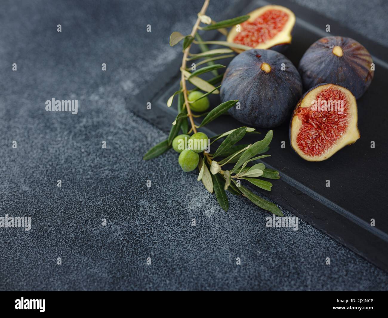 fresh ripe figs fruit and olive branch on dark table. mediterranean ...