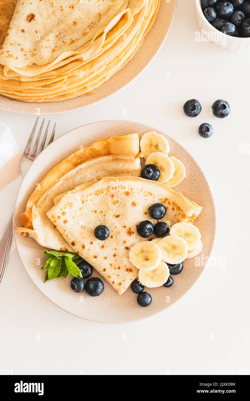 French crepes with banana and blueberries on white table. Top view ...