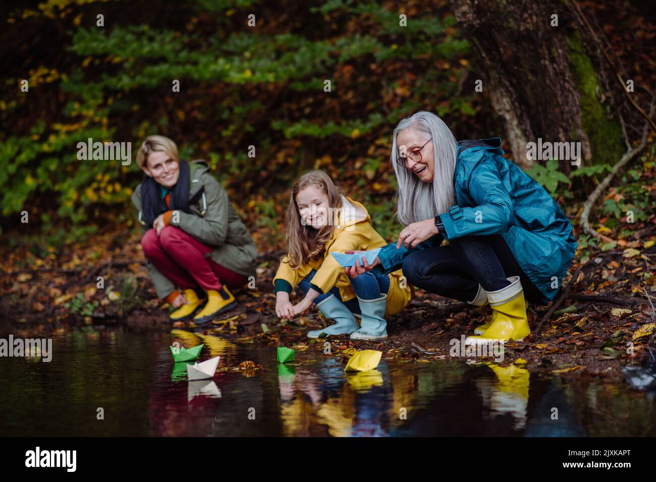 Small girl with mother and grandmother playing with paper boats in lake ...