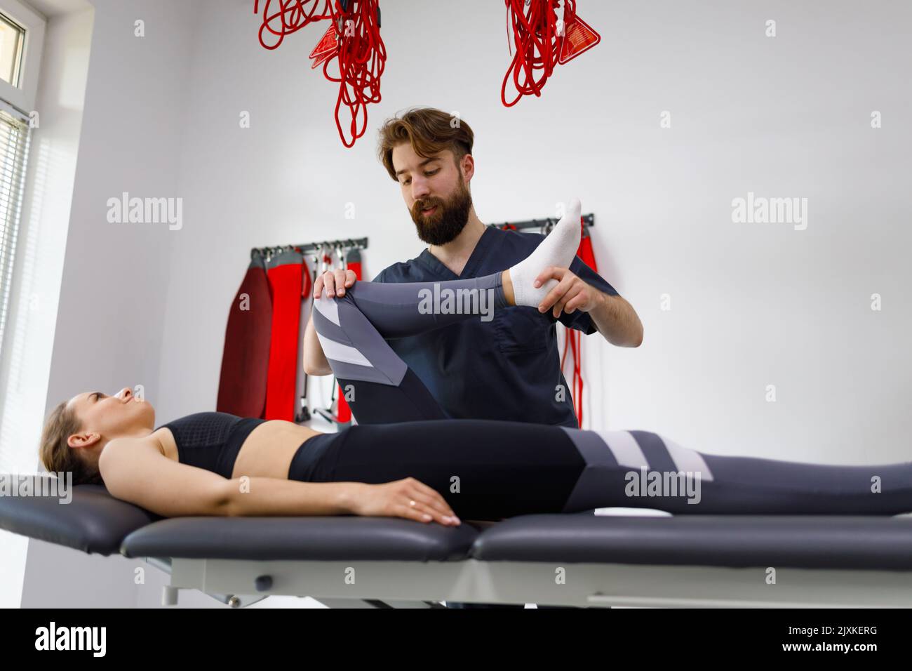 Man physiotherapist helping woman with legs exercises. Flexing patient ...