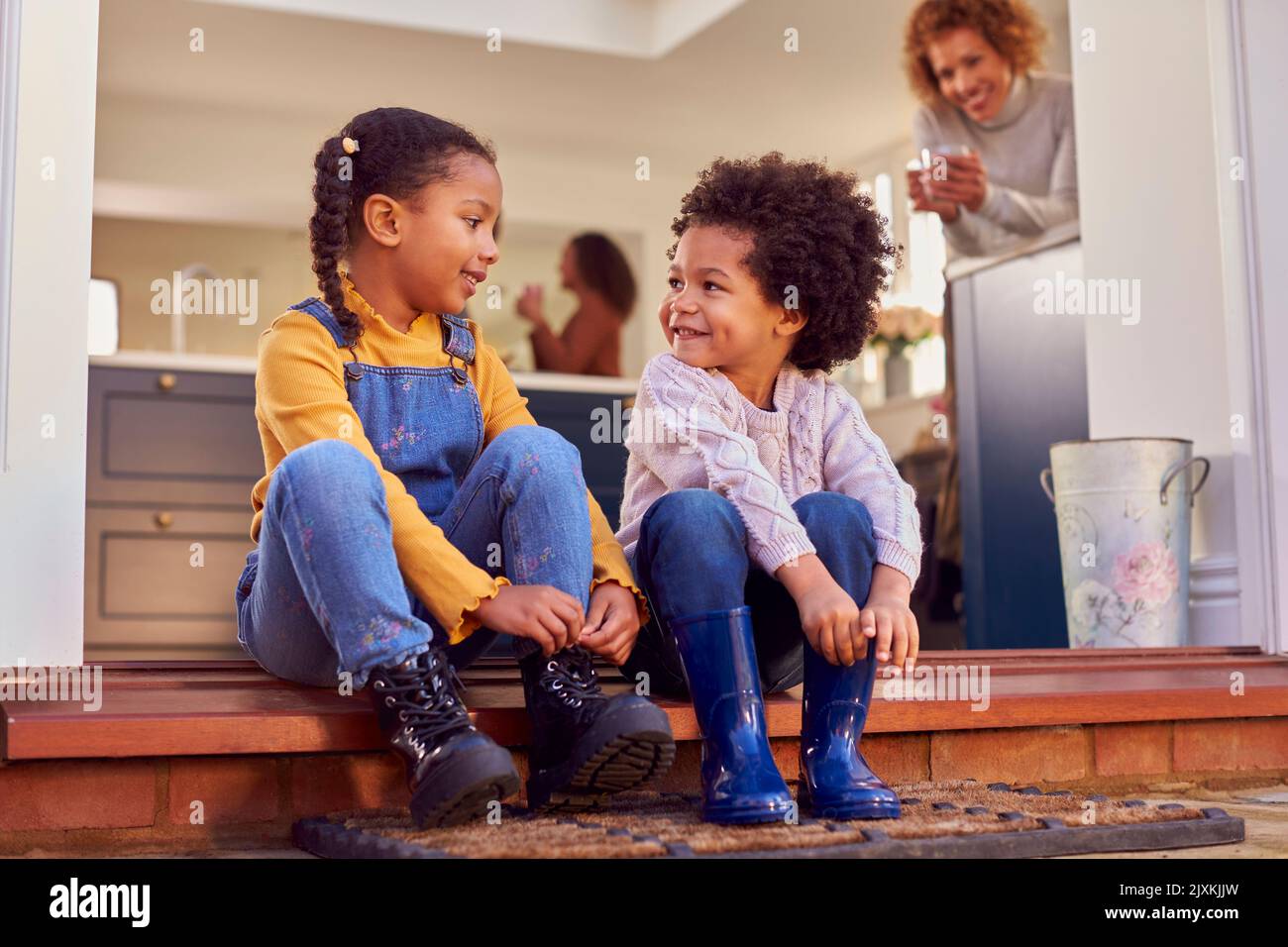 Children Sitting On Step At Home Putting On Boots Before Going On ...