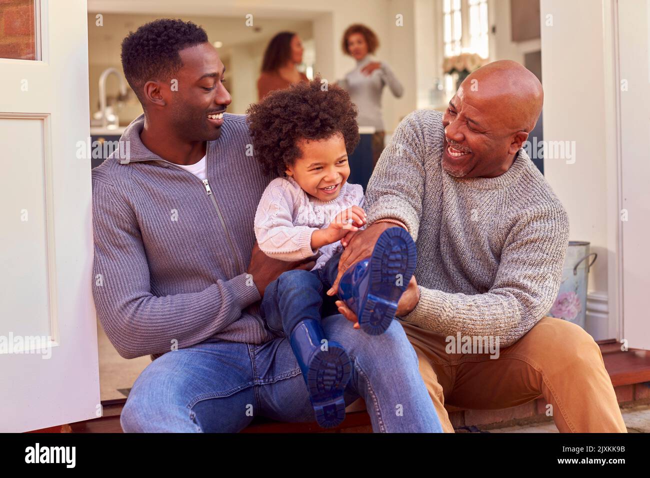 Grandfather With Father And Son Sit On Step At Home Putting On Boots ...