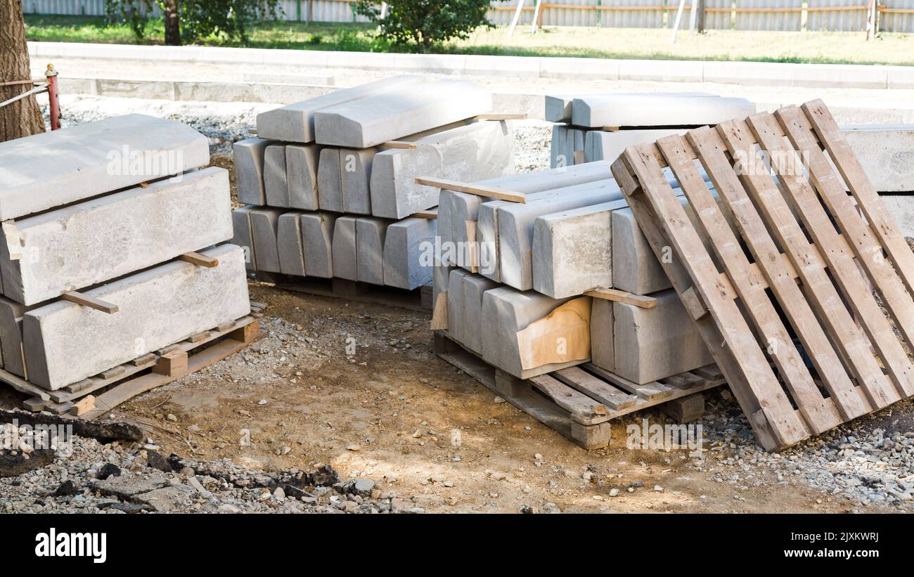 Reinforced concrete blocks neatly stacked on the territory of a fenced construction site curb ...