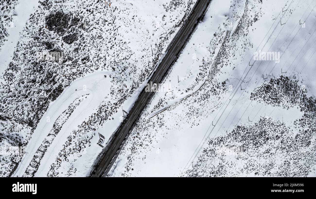 An aerial view of a car on an asphalt road going through snowy fields ...