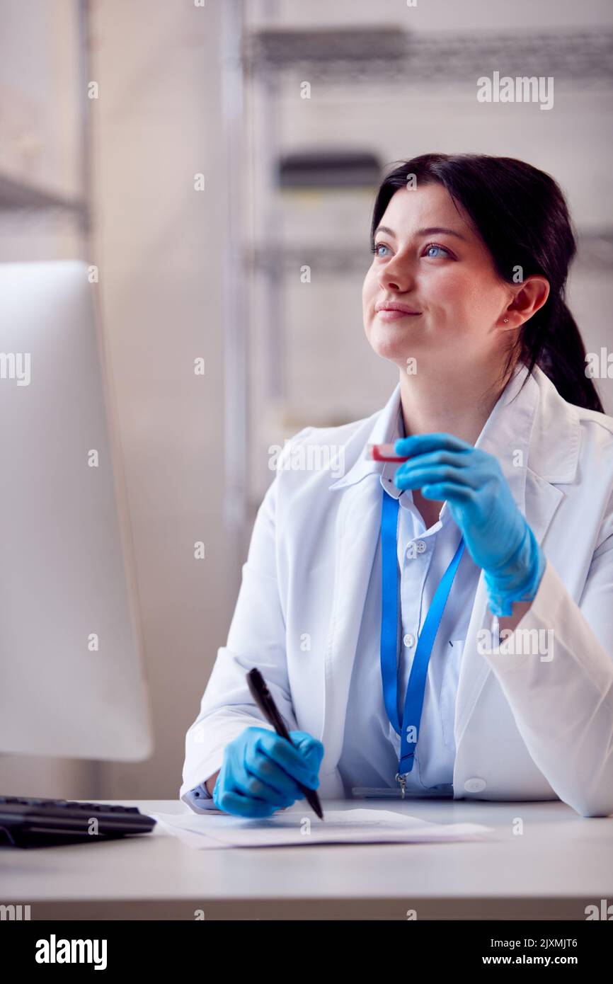 Female Lab Worker Wearing White Coat Recording Blood Test Results On ...