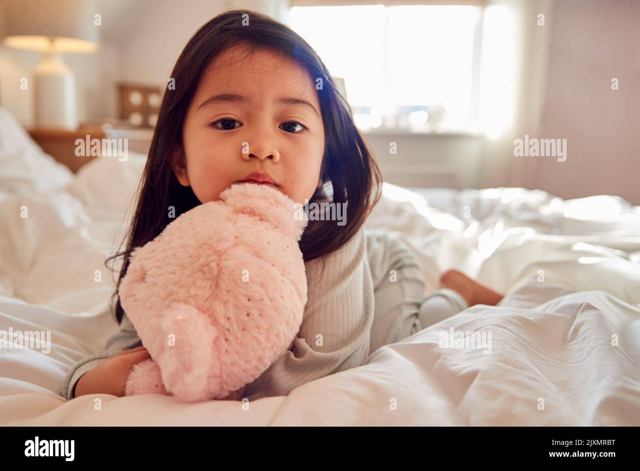 Young Girl Sitting On Bed Wearing Pyjamas At Home Cuddling Soft Toy ...