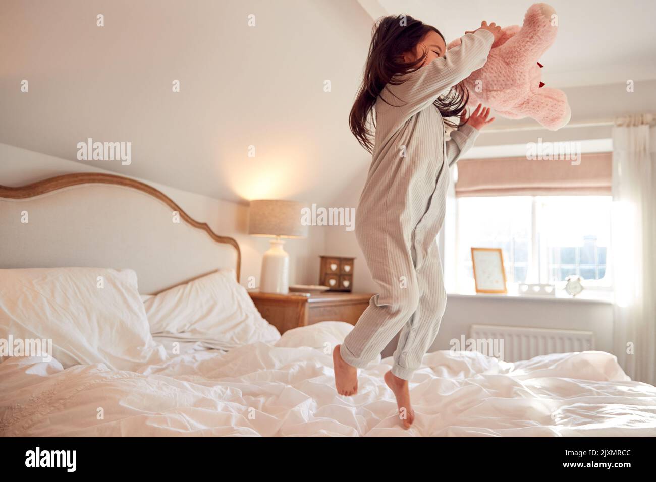 Active Young Girl Full Of Energy Jumping On Bed At Home With Soft Toy ...